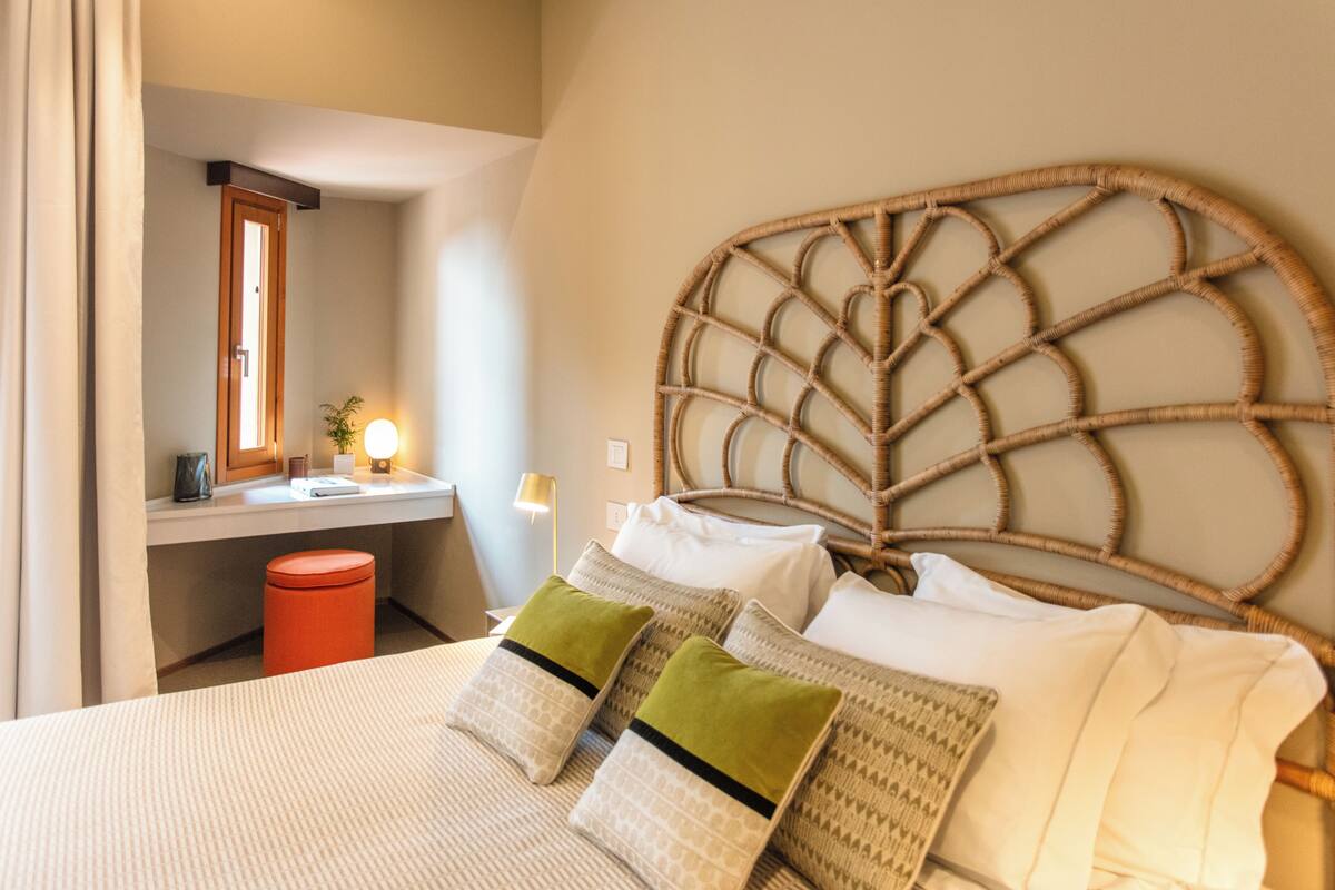 Quarto de hotel com uma cama, uma escrivaninha e um espelho.