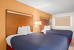 Quarto de hotel com duas camas, uma mesa de cabeceira com abajur, janela com vista e espelho na parede.