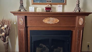 Lareira com duas luminárias de parede, um quadro emoldurado acima e um vaso com flores secas à esquerda.