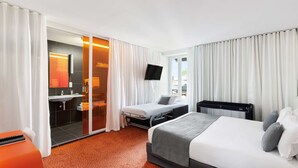 Quarto de hotel com cama, escrivaninha, televisão, porta deslizante para o banheiro e vista para o exterior.
