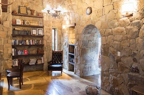 Um quarto com paredes de pedra, estantes de livros, lareira e uma cadeira de madeira.
