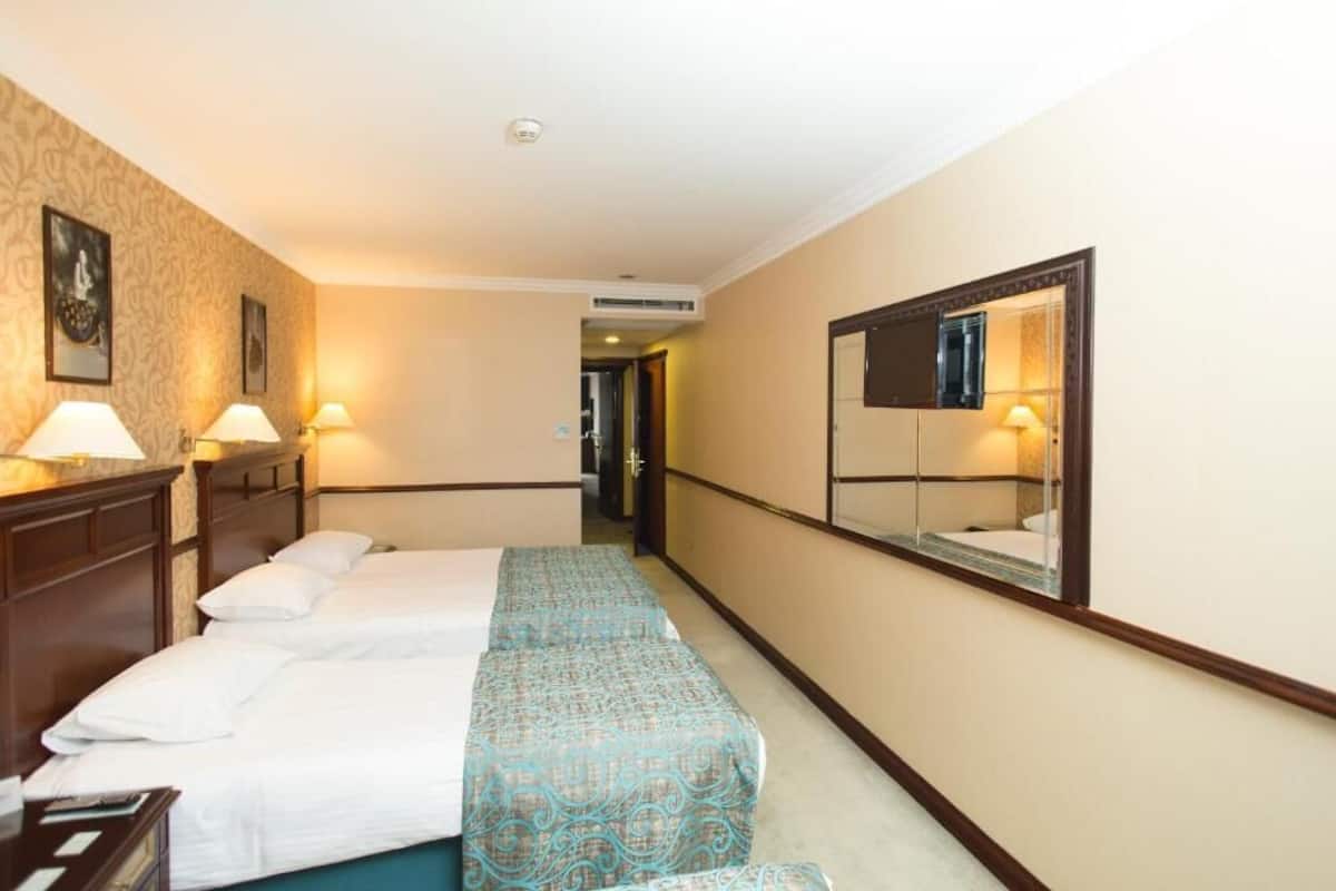 Quarto de hotel com cama, mesas de cabeceira, espelho e corredor que dá para outro quarto.