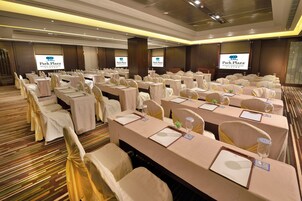 Uma sala de conferências com fileiras de mesas, cadeiras e uma grande tela exibindo o logotipo Park Plaza.