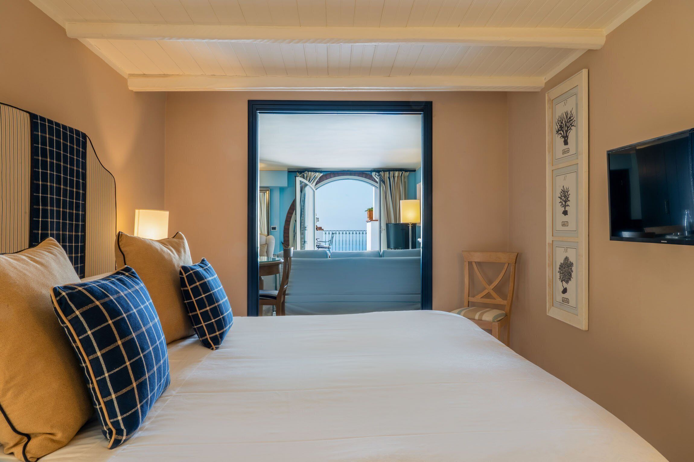 Quarto de hotel com uma cama grande, duas luminárias de cabeceira, uma televisão e vista para a varanda.