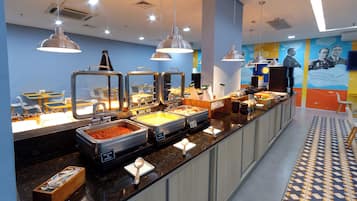 Uma área de buffet com várias estações de comida, piso estampado e parede com um mural.