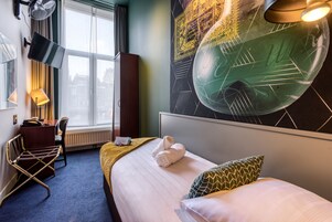 Quarto de hotel com cama, escrivaninha, cadeira, televisão e uma grande janela.