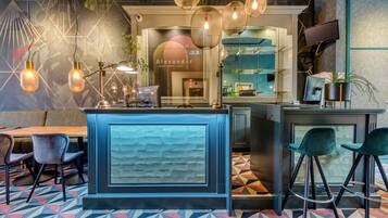 Uma área de bar moderna com balcão azul, banquetas, luminárias pendentes e piso estampado.