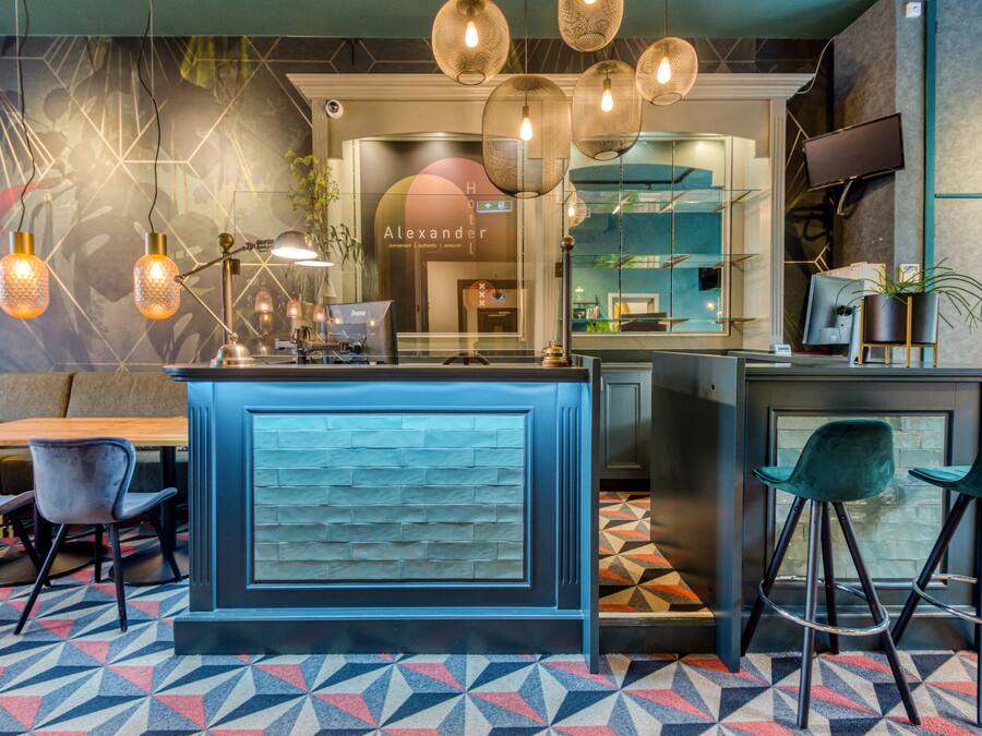 Uma área de bar moderna com balcão azul, banquetas, luminárias pendentes e piso estampado.