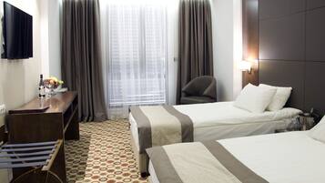 Quarto de hotel com duas camas, uma escrivaninha, uma cadeira, uma televisão e uma janela com cortinas.