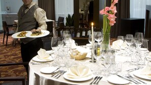 Mesa de jantar posta para refeição, com vários copos de vinho, pratos e talheres.