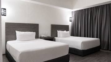 Quarto de hotel com duas camas, uma mesinha de cabeceira, um telefone e uma janela com cortinas.