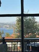 Vista da janela com varanda, com vista para um corpo de água, árvores e colinas ao longe.