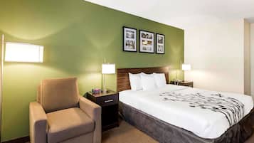 Quarto de hotel com cama, cadeira, mesa de cabeceira e luminárias fixadas na parede.