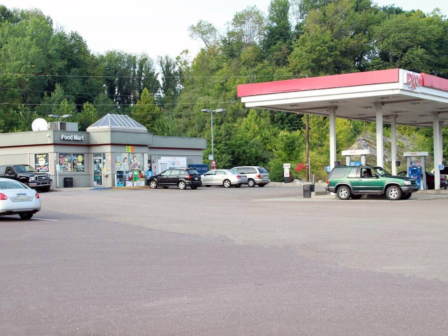 Um posto de combustível com toldo vermelho, uma loja de conveniência e vários carros estacionados.