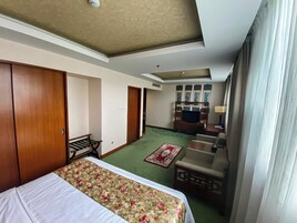 Quarto de hotel com cama, sofá, escrivaninha, televisão e janela com cortinas.