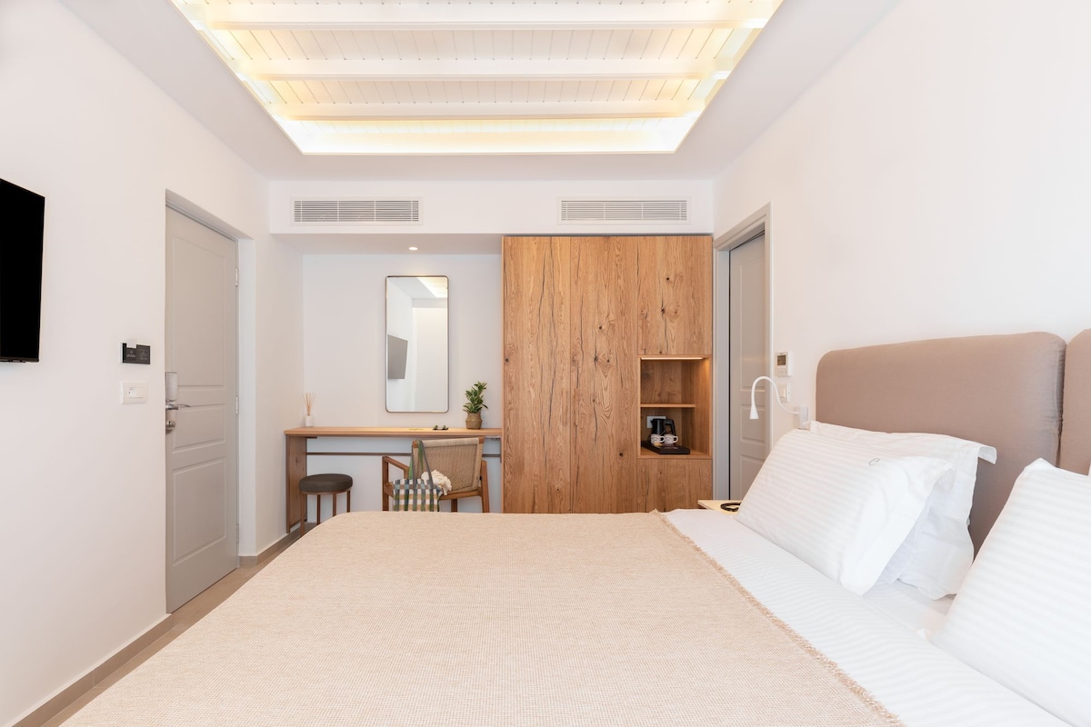 Quarto moderno com uma cama grande, um guarda-roupa de madeira, uma escrivaninha com cadeira e uma TV fixada na parede.