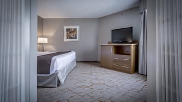 Quarto de hotel com cama, televisão em aparador de madeira, abajur e quadro na parede.
