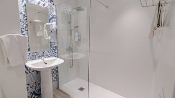 Casa de banho moderna com chuveiro envolto em vidro, lavatório pedestal branco e paredes com azulejos estampados.