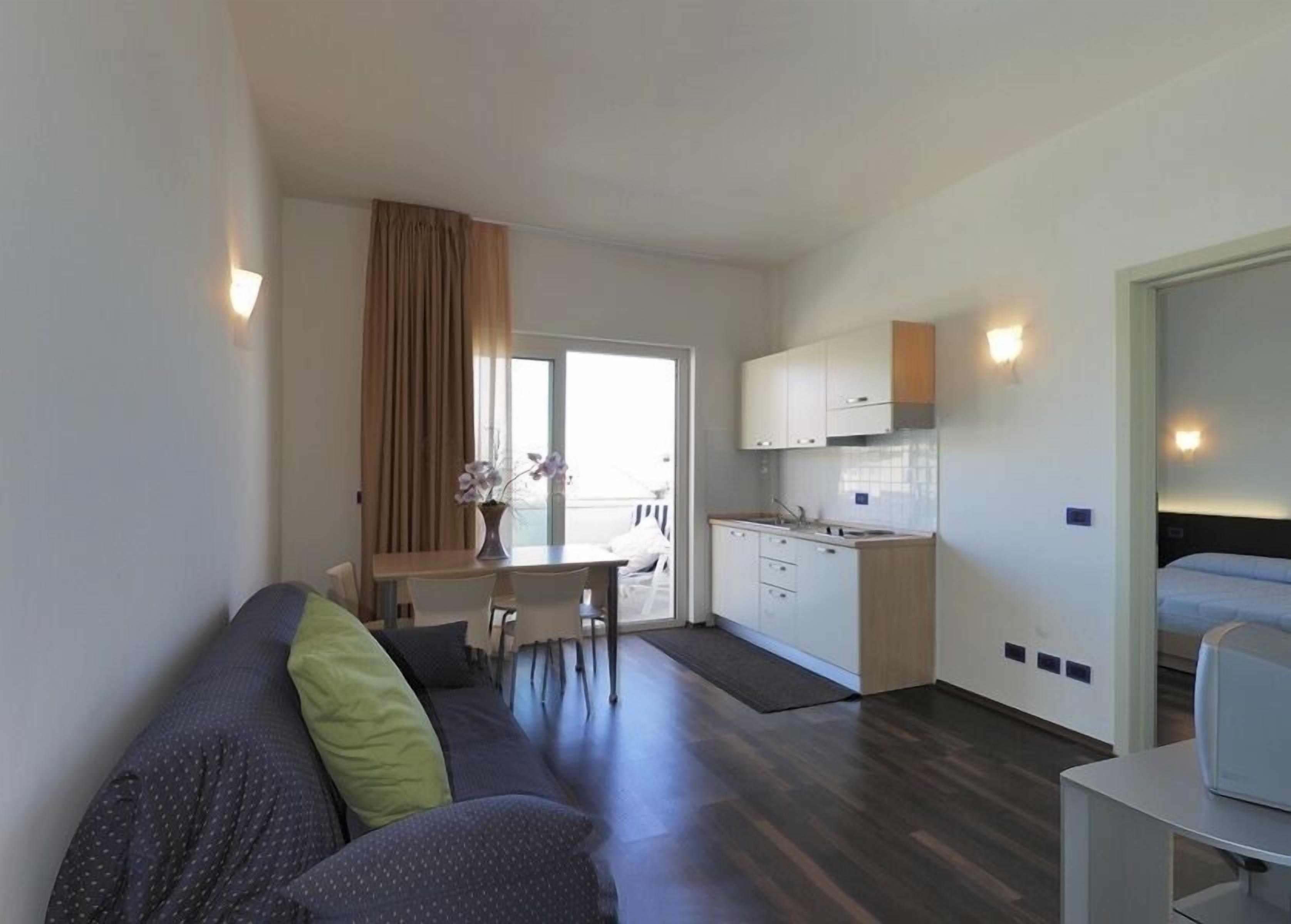 Quarto de hotel moderno com sofá, mesa de jantar e cozinha compacta.