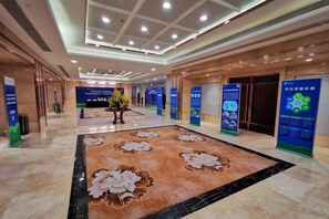 Um hall de hotel com piso de mármore, balcão de recepção e cartazes informativos.
