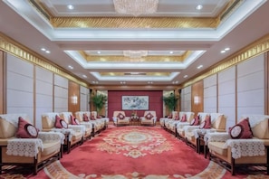 Uma sala de conferências com fileiras de cadeiras, um tapete vermelho e um candelabro.