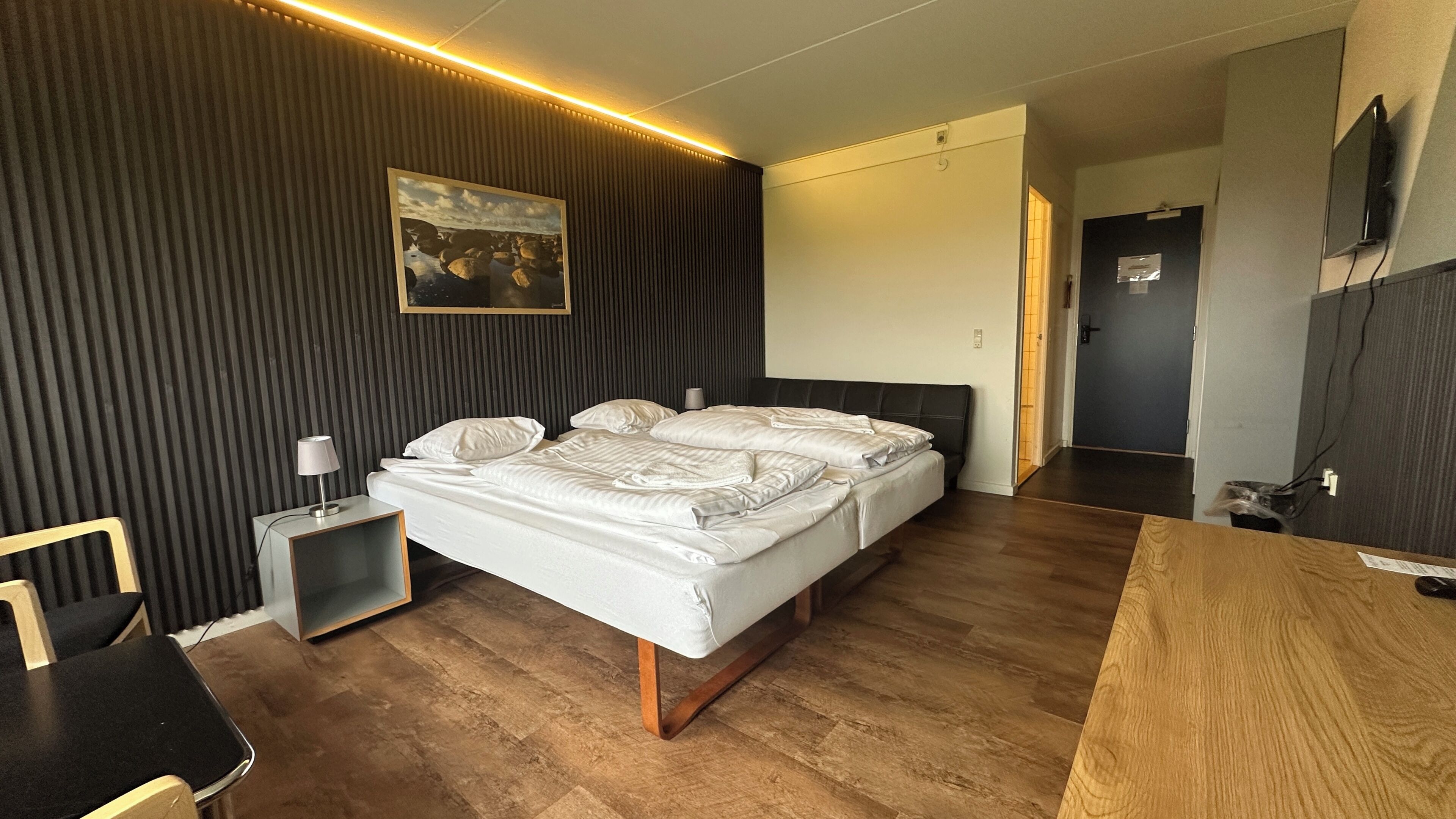 Quarto de hotel moderno com uma cama grande, mesas de cabeceira, uma escrivaninha e uma televisão.