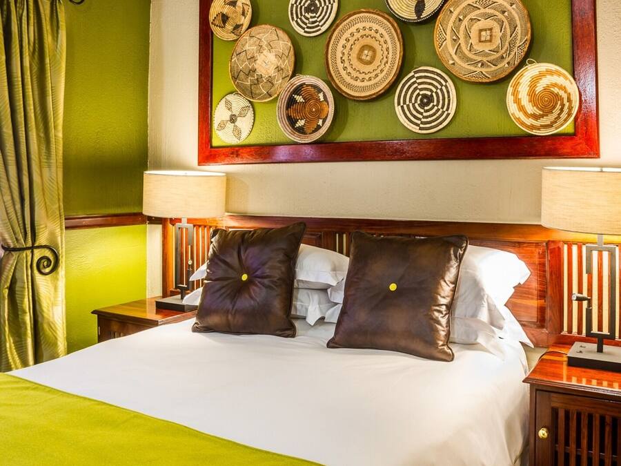 Quarto de hotel com uma cama, duas mesas de cabeceira, uma luminária na parede e uma cortina verde.