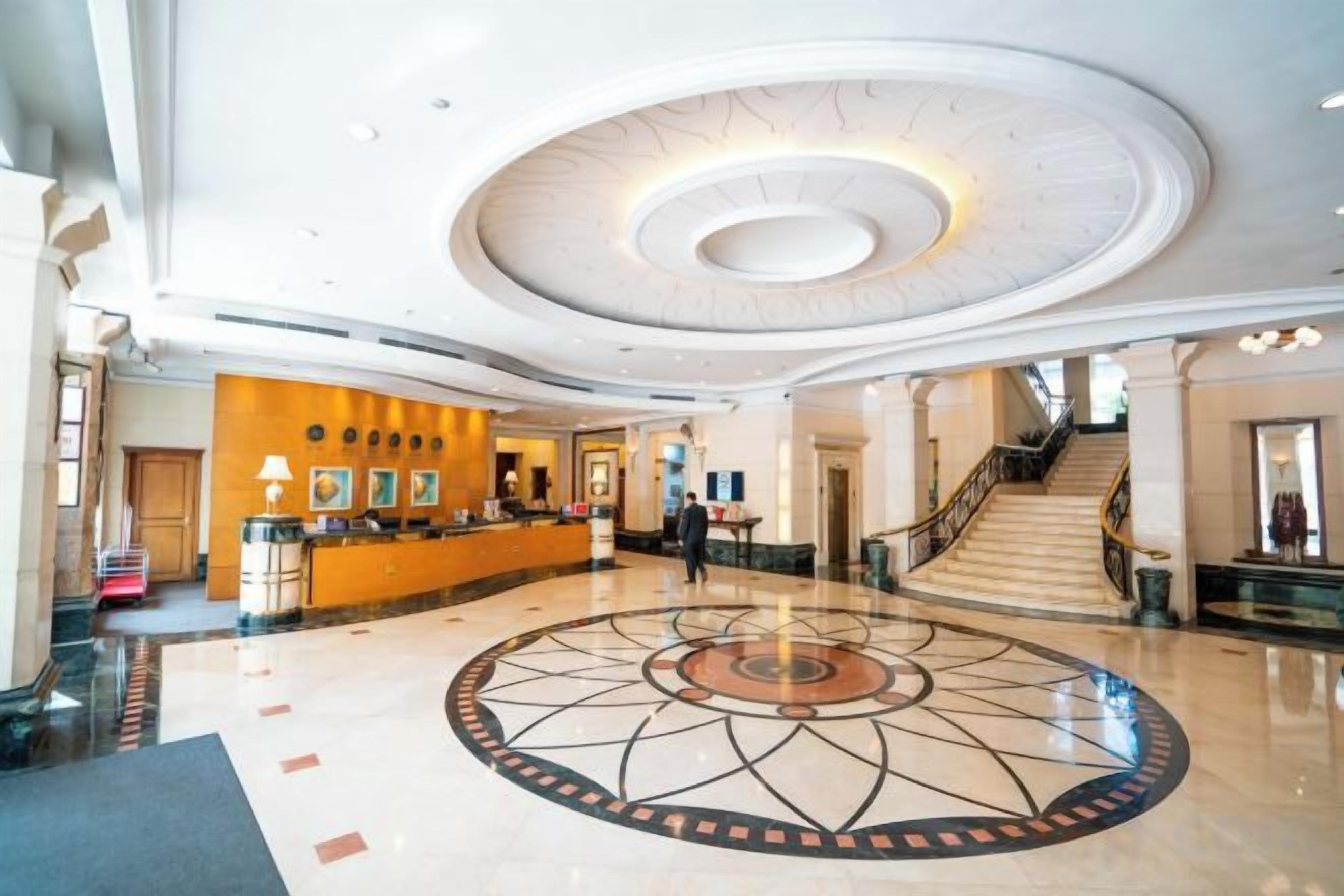 Um saguão de hotel com um design circular no chão, uma mesa de recepção e uma escadaria.