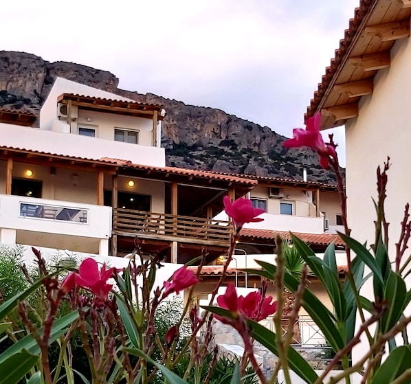 Um edifício com vários andares e varanda, cercado por vegetação e montanhas ao fundo.