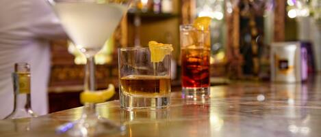 Um bar com bancada polida, um copo de martini, um copo highball e um coquetel com rodela de limão.