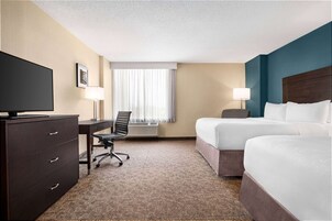 Quarto de hotel com cama, escrivaninha, cadeira, televisão e janela com cortinas.