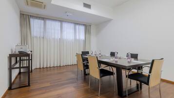 Uma sala de conferências com uma mesa comprida, quatro cadeiras, uma mesinha lateral e uma janela com cortinas.