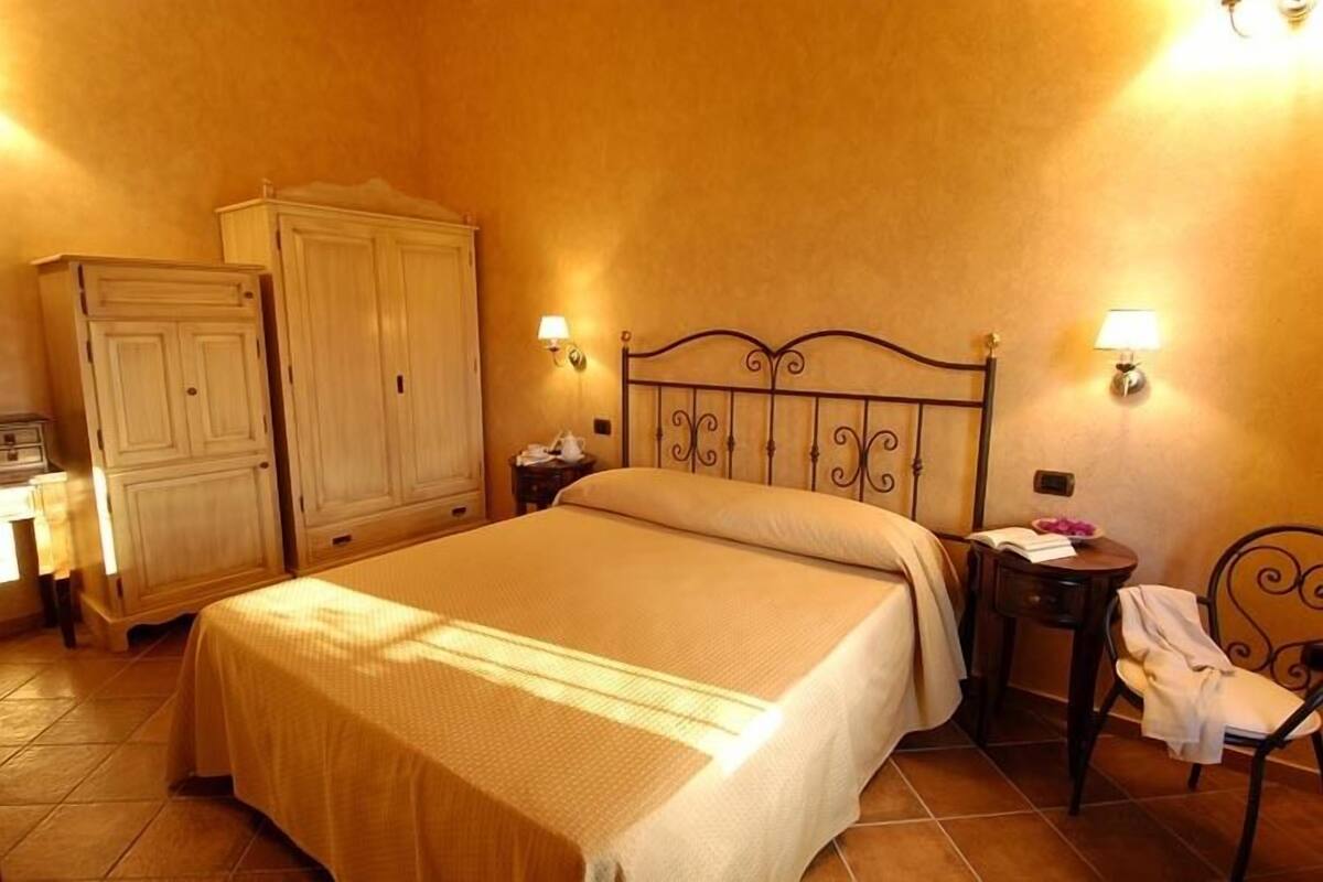 Quarto com cama, guarda-roupa, mesa de cabeceira e duas luminárias de parede.