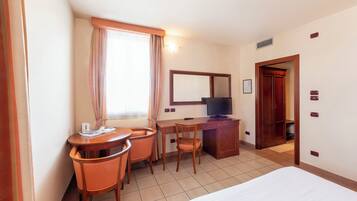 Quarto de hotel com cama, escrivaninha com cadeira, televisão e guarda-roupa.