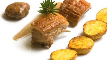 Prato de carne de porco assada com um ramo de alecrim, acompanhado de batatas rústicas.