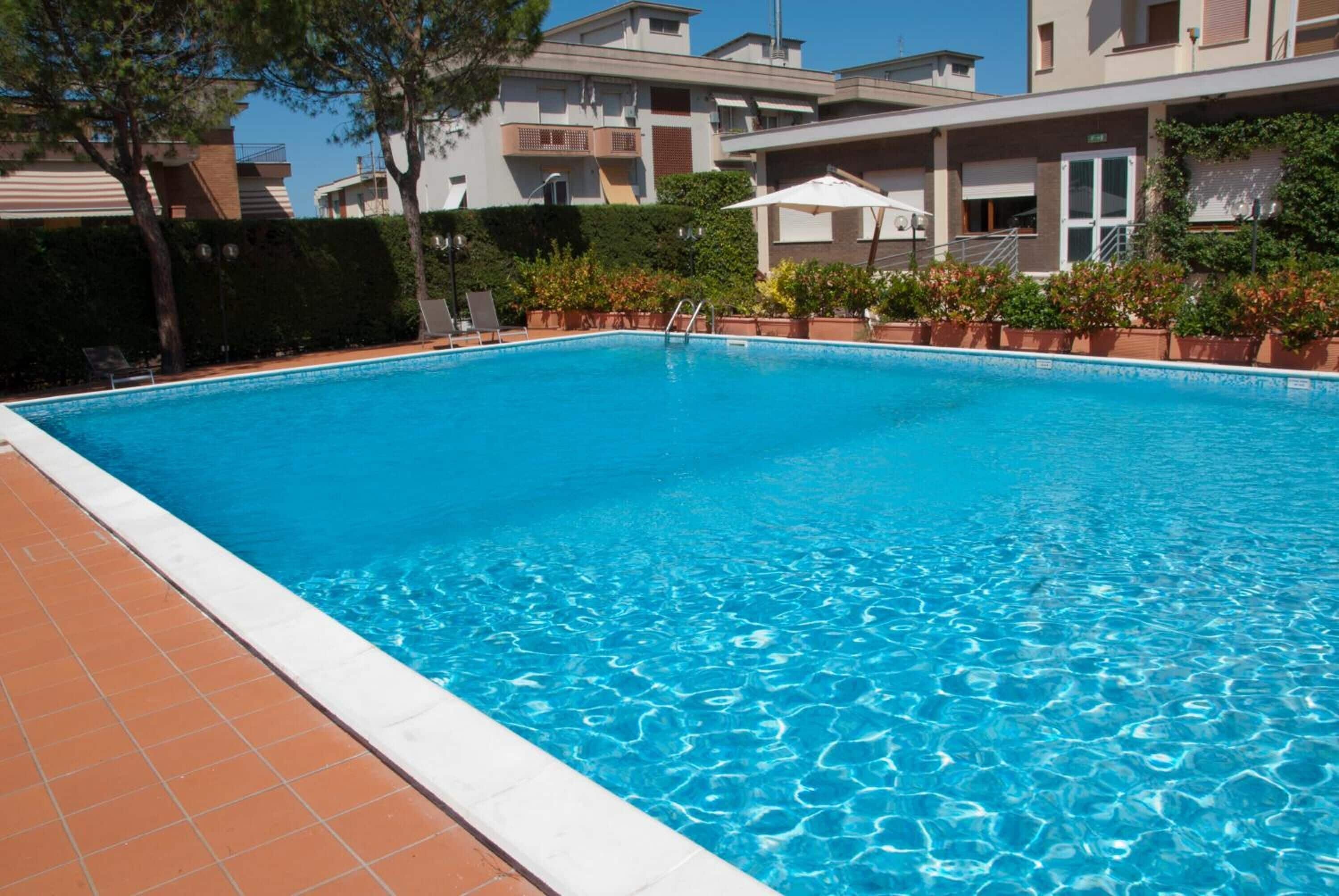 Uma piscina retangular com água azul cristalina, rodeada por um deck revestido de azulejos.