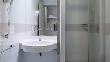 Uma casa de banho moderna com uma sanita branca, secador de cabelo e cabine de duche em vidro.