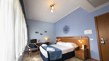 Quarto de hotel com cama, escrivaninha, cadeira e televisão.