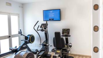 Ginásio com equipamentos de cardio, uma TV exibindo uma mensagem de boas-vindas e uma grande janela.