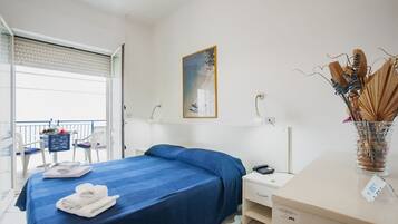 Quarto de hotel com cama, escrivaninha, cadeira, pequena mesa com um vaso e vista para a varanda.