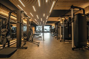 Academia com diversos equipamentos de exercício, um banco e espelho fixado na parede.