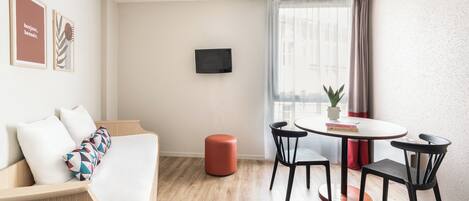 Uma sala de estar moderna com sofá, puf e área de jantar com cadeiras e mesa.