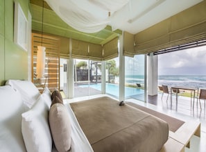Quarto com uma cama grande, vista para o oceano e varanda com mobiliário de exterior.