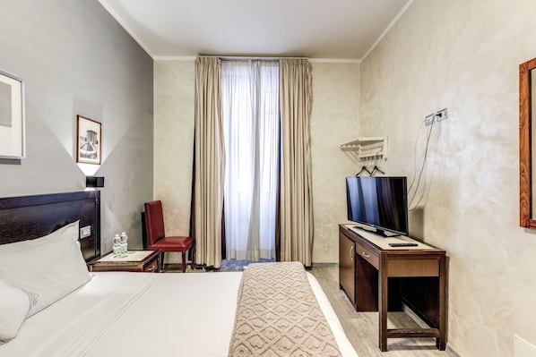 Quarto de hotel com cama, escrivaninha, cadeira, televisão e janela com cortinas.