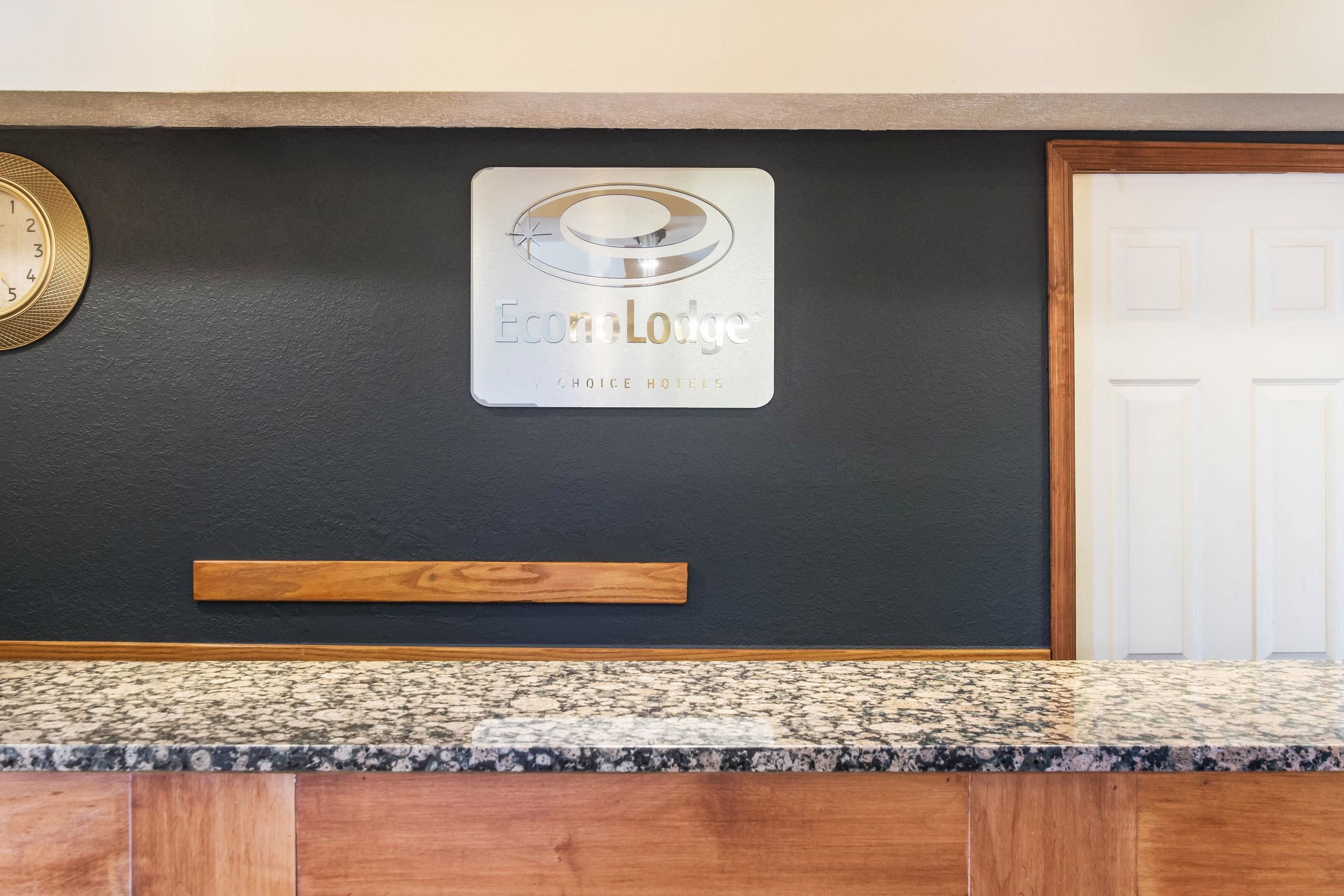 Uma área de recepção com um letreiro para 'Ecom Lodge Choice Hotels' na parede, um painel de madeira abaixo do letreiro e um balcão de mármore.
