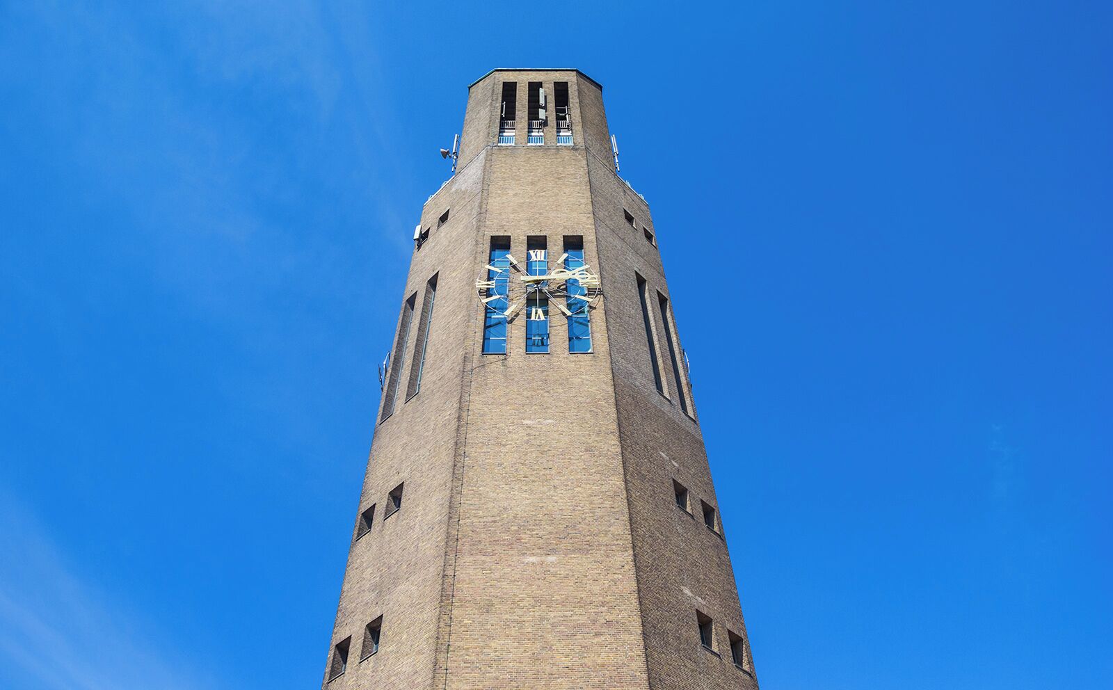 Uma torre de tijolos alta, com um grande relógio e várias janelas.