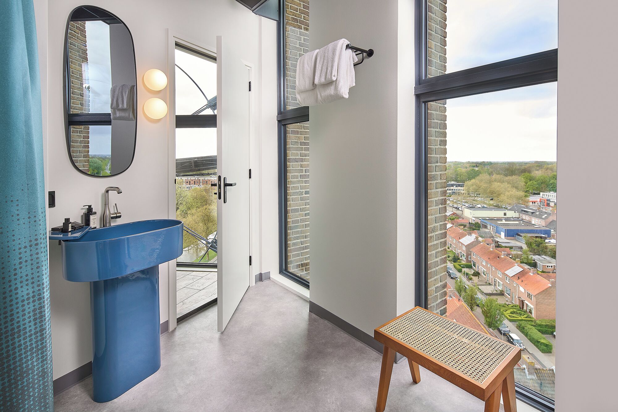 Uma casa de banho com uma pia azul, um espelho, um porta-toalhas e vista para uma área residencial através de uma janela ampla.
