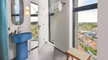 Uma casa de banho com uma pia azul, um espelho, um porta-toalhas e vista para uma área residencial através de uma janela ampla.