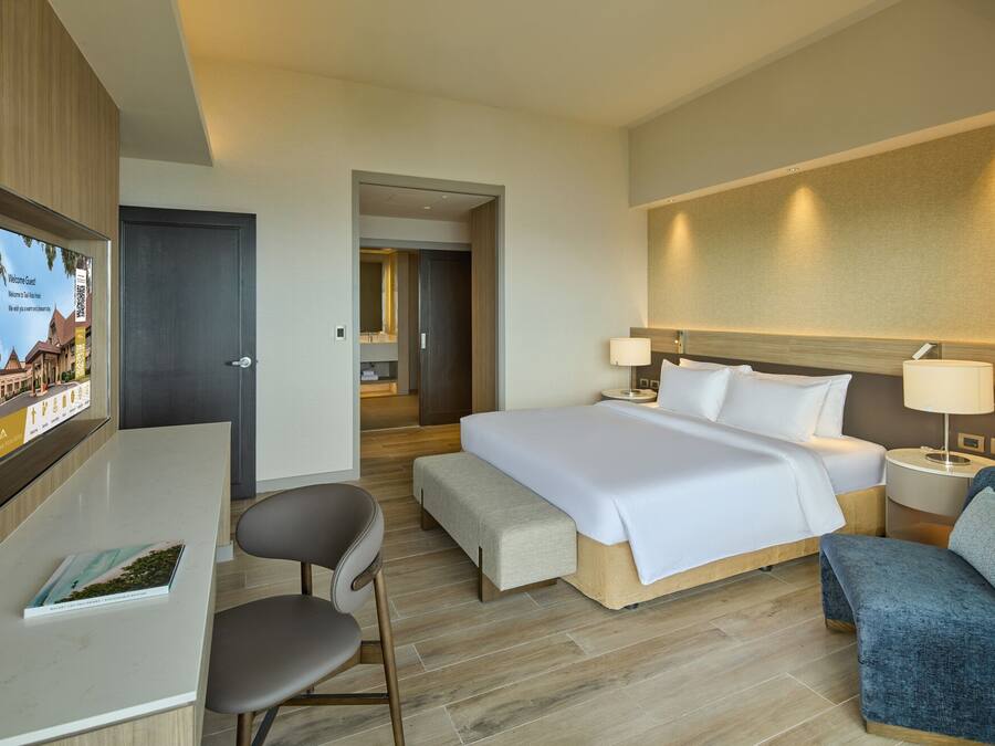 Quarto de hotel com cama, mesas de cabeceira, escrivaninha e uma cadeira.