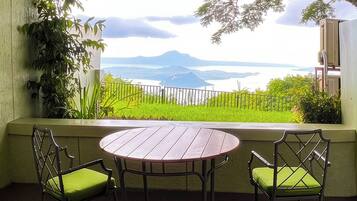 Uma varanda com mesa e cadeiras, vista para uma paisagem montanhosa e um corpo d'água.